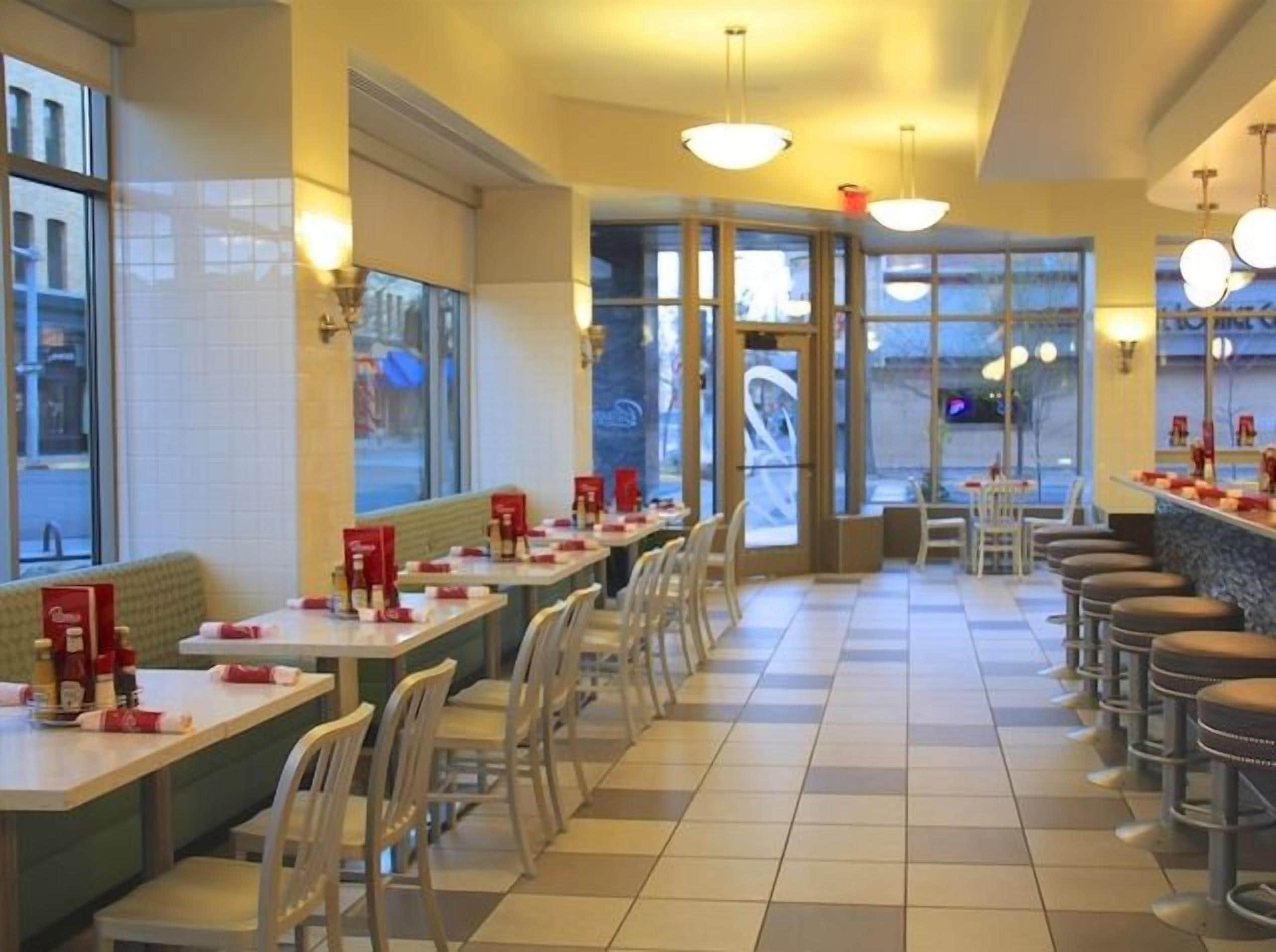 Um restaurante com um balcão comprido, várias mesas e cadeiras.