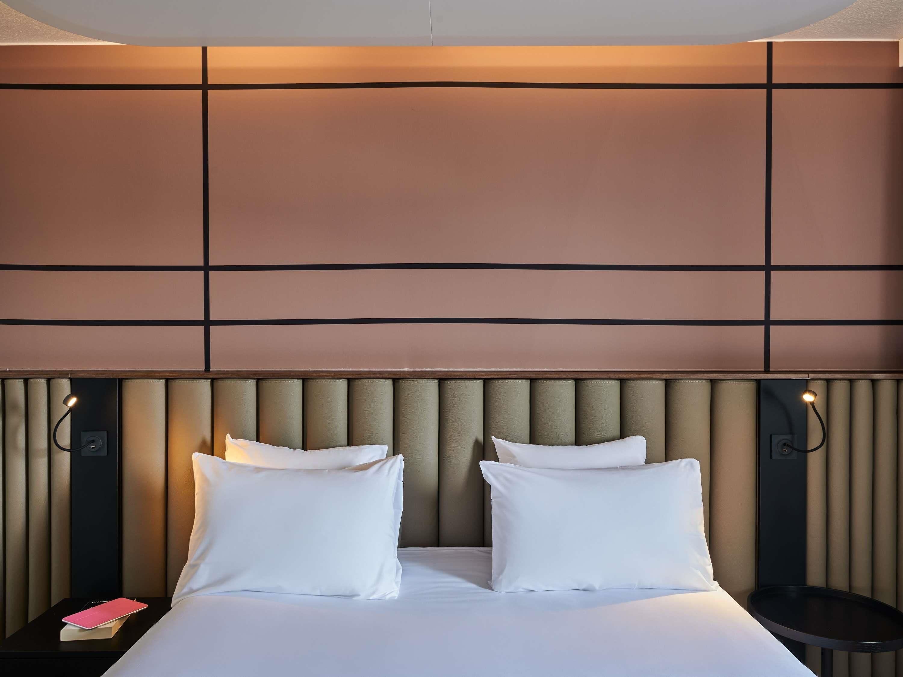 Quarto de hotel com uma cama grande, duas mesas de cabeceira e uma cabeceira com padrão quadriculado.