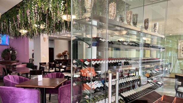 Restaurante com plantas pendentes, espaço para exibição de vinhos e cadeiras roxas.