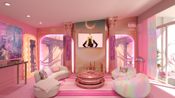 Quarto luxuoso com mesa redonda central, assentos confortáveis e uma tela grande exibindo uma pessoa.