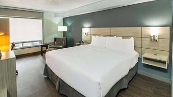 Quarto de hotel com uma cama grande, uma escrivaninha com luminária, uma cadeira e uma mesa de cabeceira com telefone.