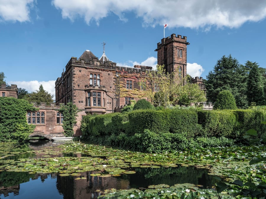 Um edifício histórico com uma torre, rodeado por um lago com nenúfares e vegetação exuberante.