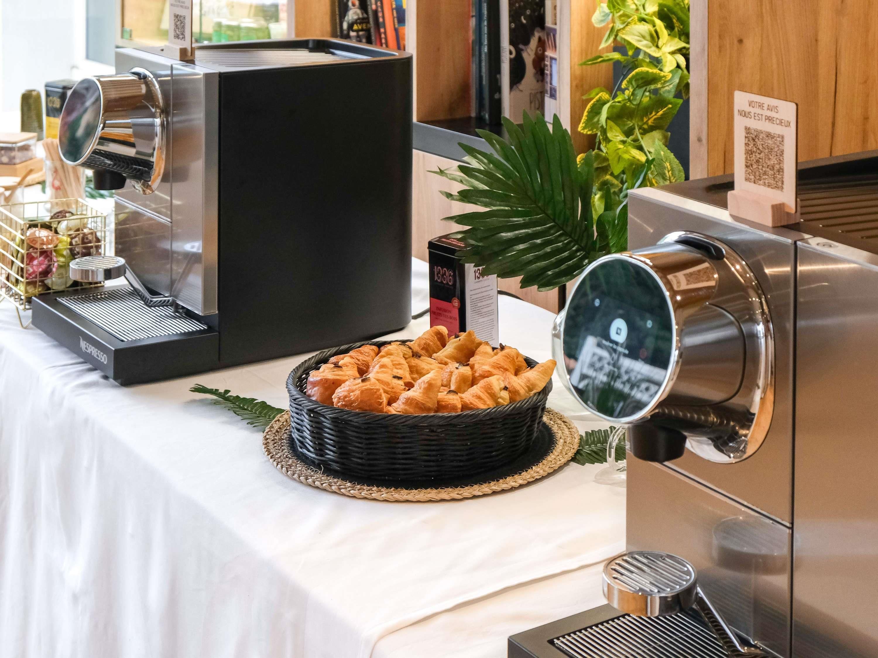 Disposição de buffet com uma cesta de croissants, uma máquina de café e um sinal com código QR.