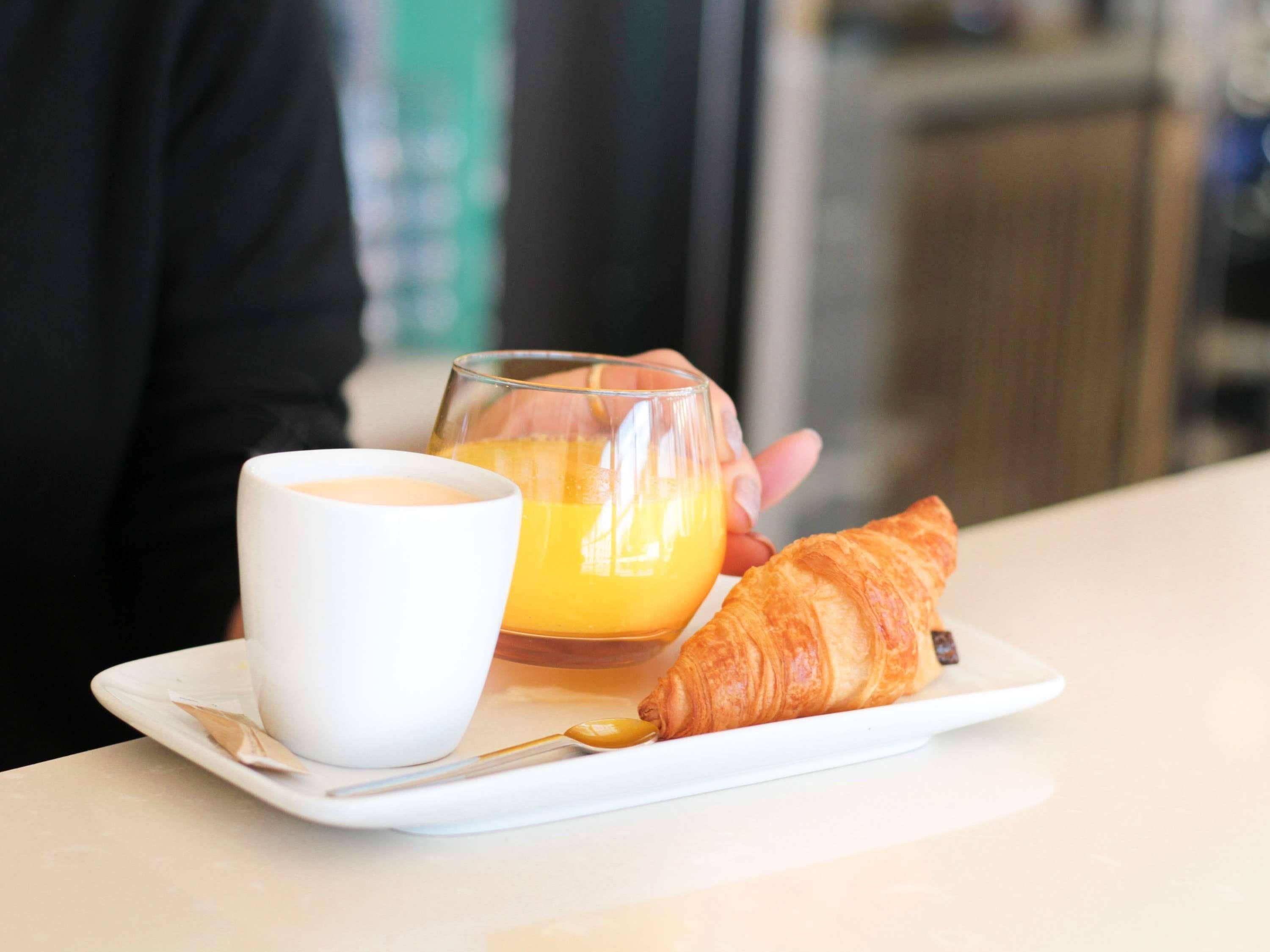 Bandeja de café da manhã com um croissant, uma xícara de café e um copo de suco de laranja em uma mesa.