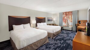 Quarto de hotel com duas camas, uma escrivaninha, uma televisão e uma janela com cortinas.