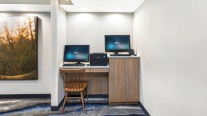 Um espaço de escritório moderno com dois computadores sobremesa, uma escrivaninha de madeira, uma cadeira e uma moldura grande na parede.