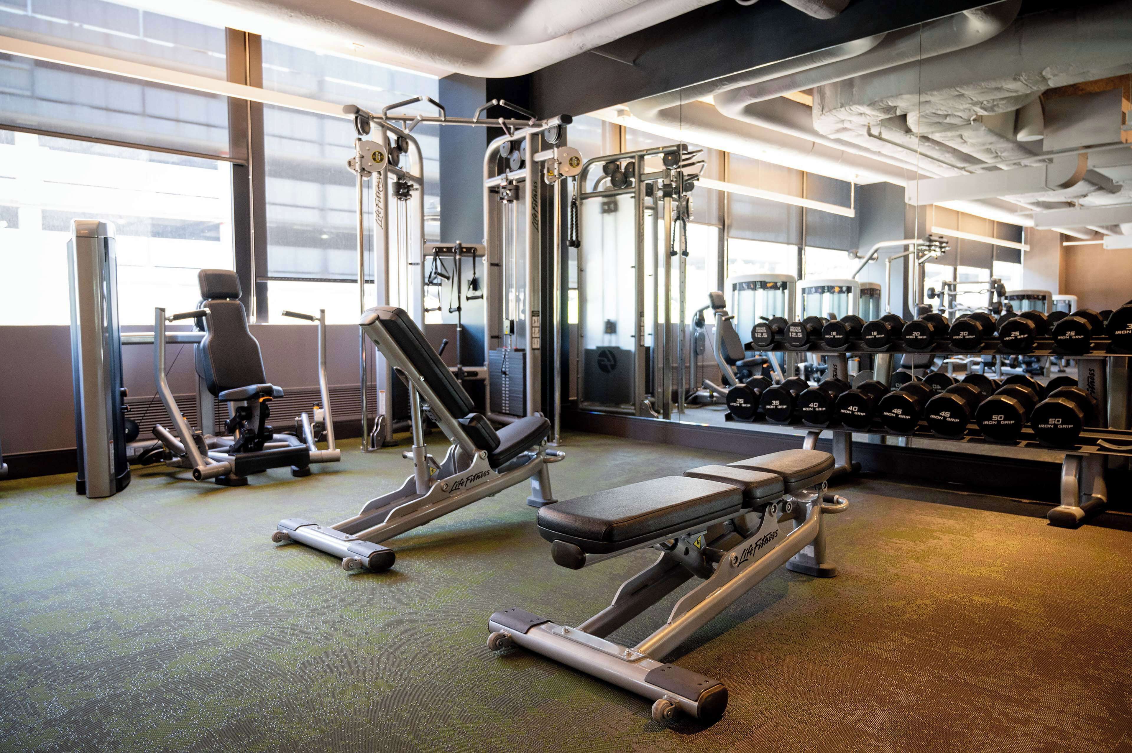 Uma academia com equipamentos de exercícios, suportes para pesos e uma grande janela.