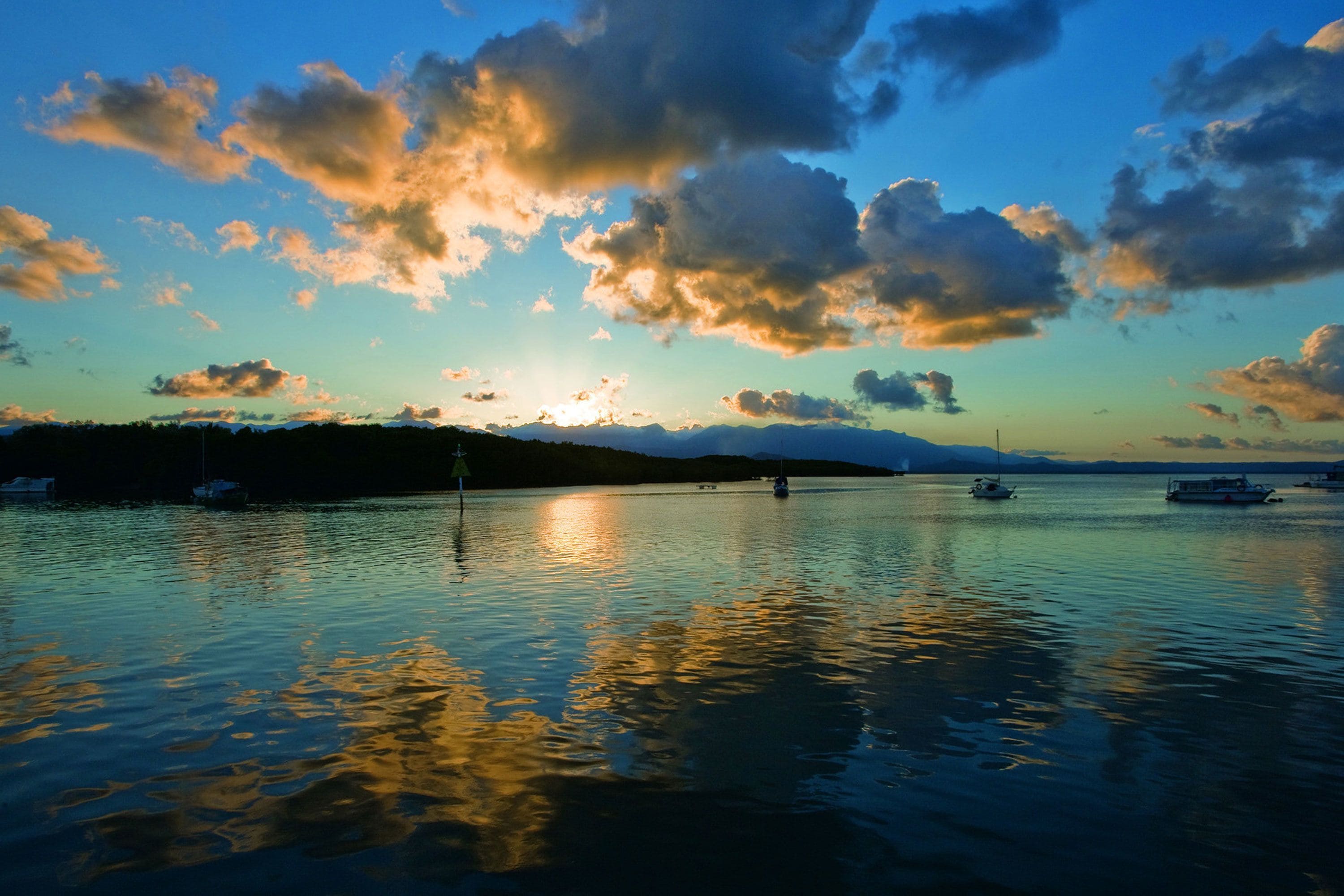 Um lago tranquilo ao pôr do sol, com barcos e uma linha de costa distante.