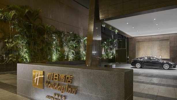 Entrada de um hotel com uma placa indicando "Holiday Inn" e "GOLDEN MILE HONG KONG".