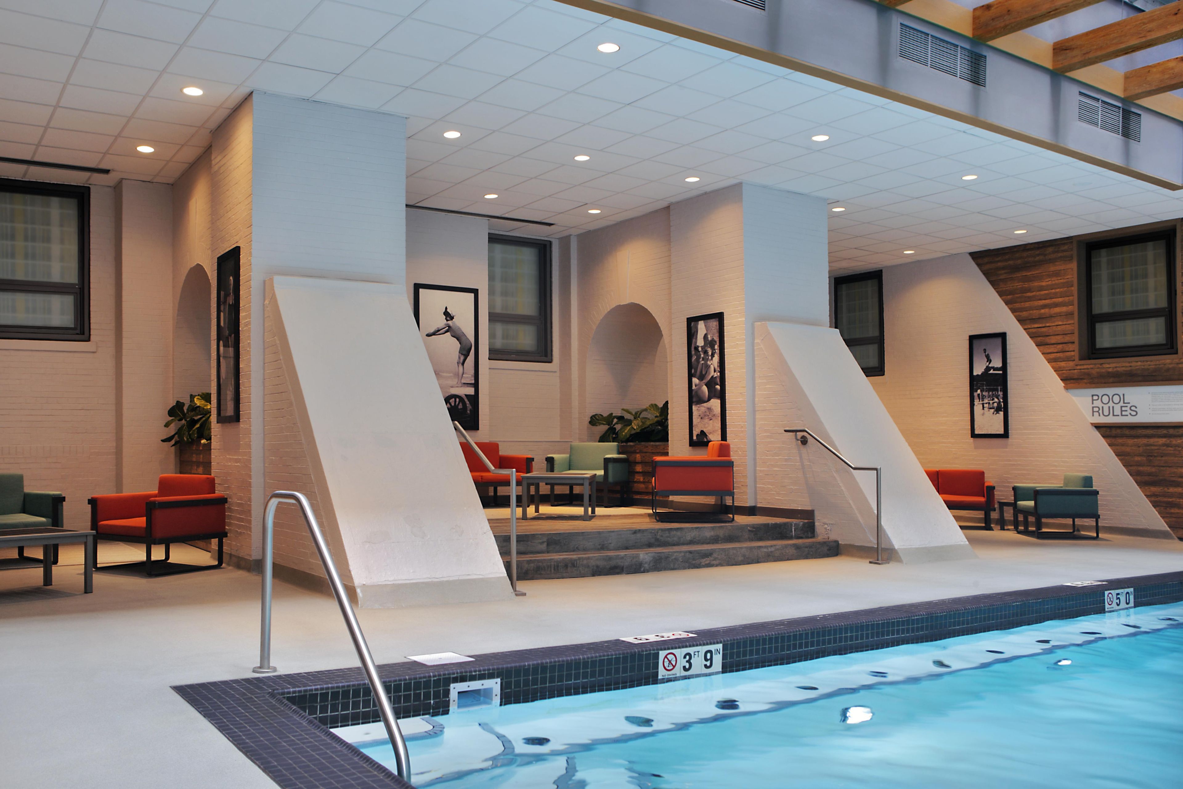 Área interna de piscina moderna, com piscina transparente, assentos e placa indicando limite de profundidade de 1,10 metros.