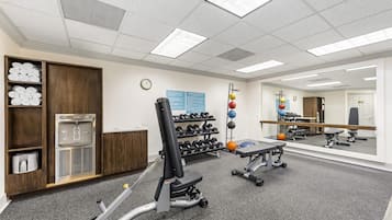 Uma academia com equipamentos de exercícios, bebedouro e espelho.