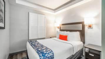 Quarto de hotel com cama, mesas de cabeceira, persianas na janela e luminária fixada na parede.