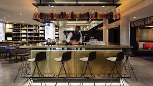 Uma área de bar com banquetas, um bartender e prateleiras cheias de garrafas.