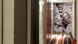 Um corredor com carpete listrado, um mural na parede e uma porta com faixa vermelha.