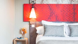 Quarto moderno com cama, mesa de cabeceira e um quadro abstrato vermelho acima da cama.
