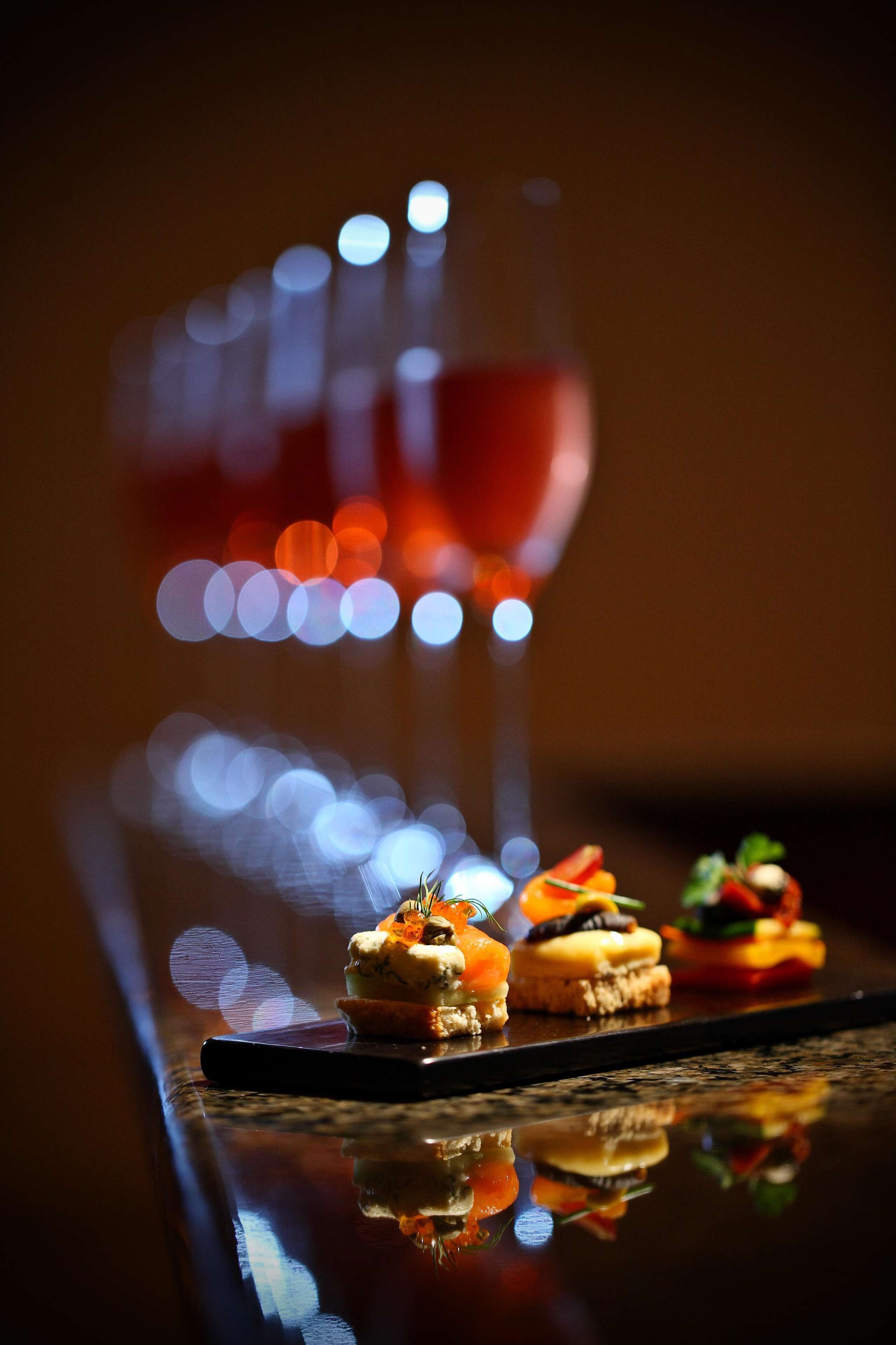 Uma mesa de sobremesas com vários pratos pequenos, um copo de vinho tinto e um fundo desfocado com luzes bokeh.