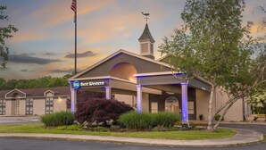 Um Western Inn com área externa coberta, um mastro com a bandeira americana e um pináculo de igreja ao fundo.
