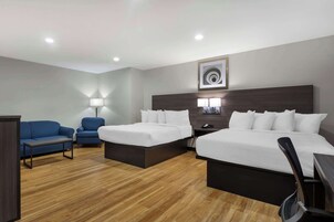 Quarto de hotel com duas camas, um sofá, uma escrivaninha e uma luminária.