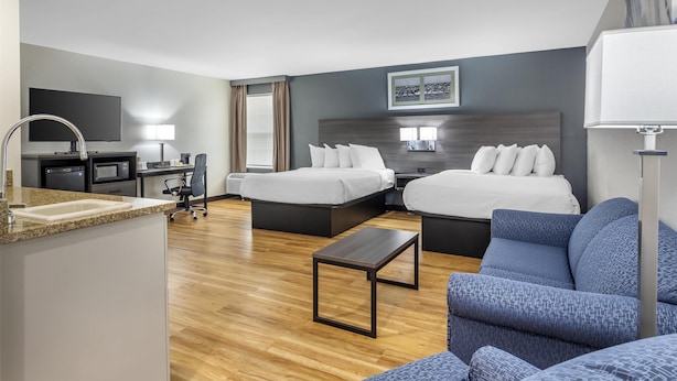 Quarto de hotel com duas camas, uma escrivaninha, uma cadeira, uma mesinha, televisão e banheiro.