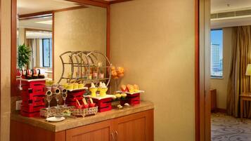 Quarto de hotel com bancada de café da manhã, com tigela de frutas, espaço para café e suporte para copos.