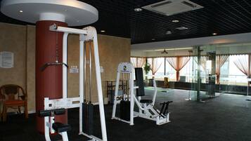 Uma academia com equipamentos de exercício, uma cadeira de madeira e um painel de vidro.
