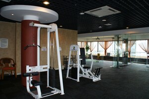 Uma academia com equipamentos de exercício, uma cadeira de madeira e um painel de vidro.