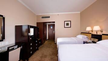 Quarto de hotel com duas camas, uma escrivaninha com cadeira, cômoda, televisão e um quadro na parede.