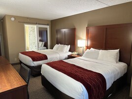 Quarto de hotel com duas camas, uma escrivaninha, uma cadeira, um abajur e um telefone.