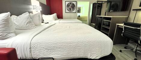 Quarto de hotel com duas camas, uma mesa, uma cadeira, uma televisão e uma parede de destaque vermelha.