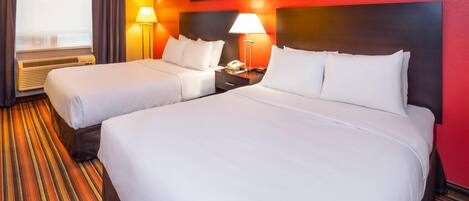 Quarto de hotel com duas camas, uma mesinha de cabeceira com abajur e uma janela com cortinas.