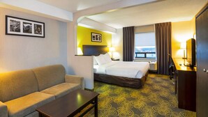 Quarto de hotel com cama, sofá, mesa de centro, televisão e janela com cortinas.