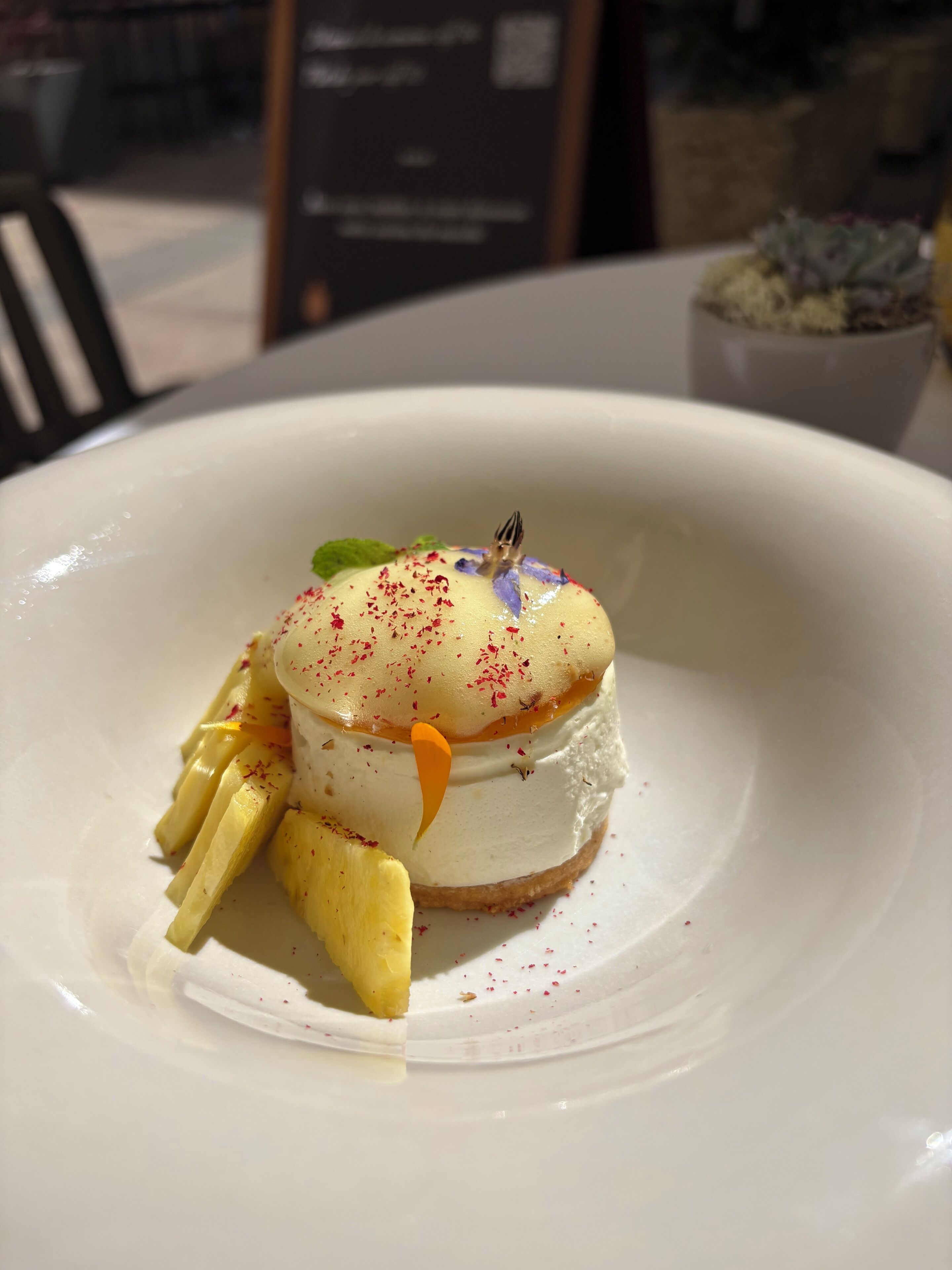 Uma sobremesa em um prato branco com guarnição, uma pequena tigela de molho e um letreiro de menu ao fundo.