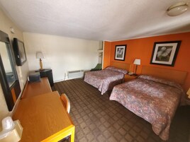Quarto de hotel com duas camas, uma escrivaninha, uma cadeira, uma televisão e um aquecedor.