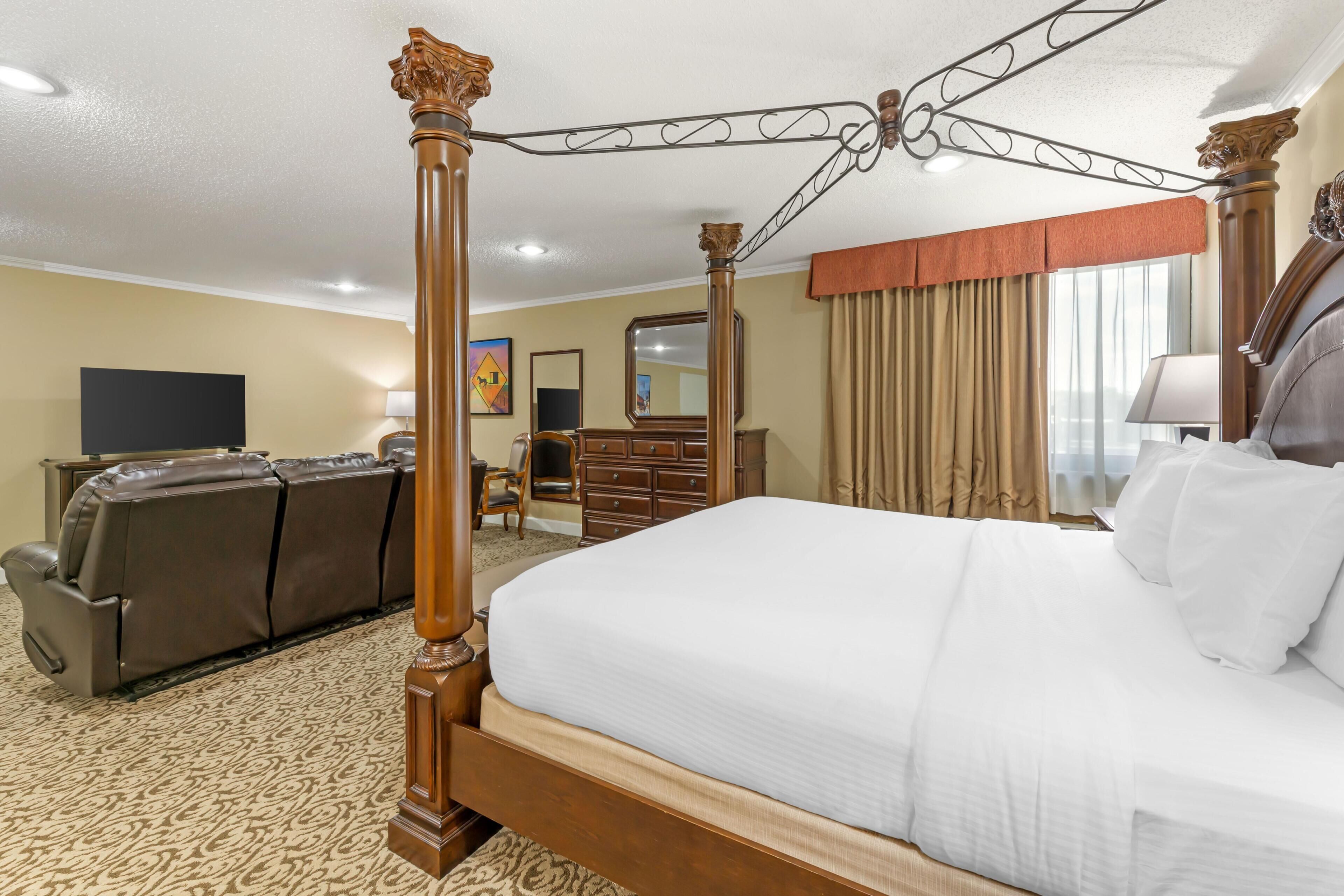 Quarto de hotel com cama de dossel, sofá, cômoda e televisão.