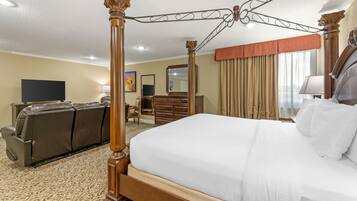 Quarto de hotel com cama de dossel, sofá, cômoda e televisão.