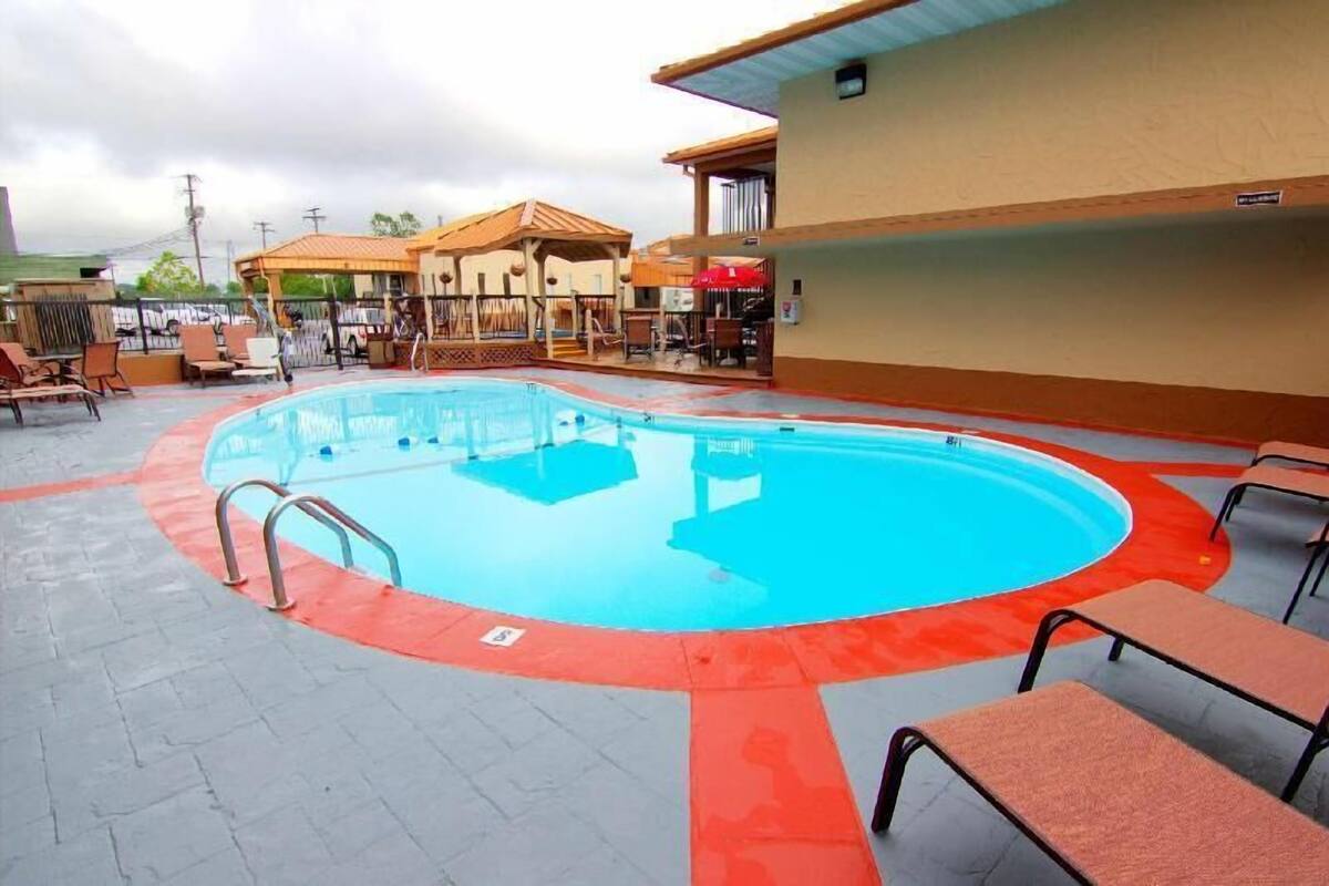 Piscina com borda vermelha, cadeiras de descanso e área de estar coberta.