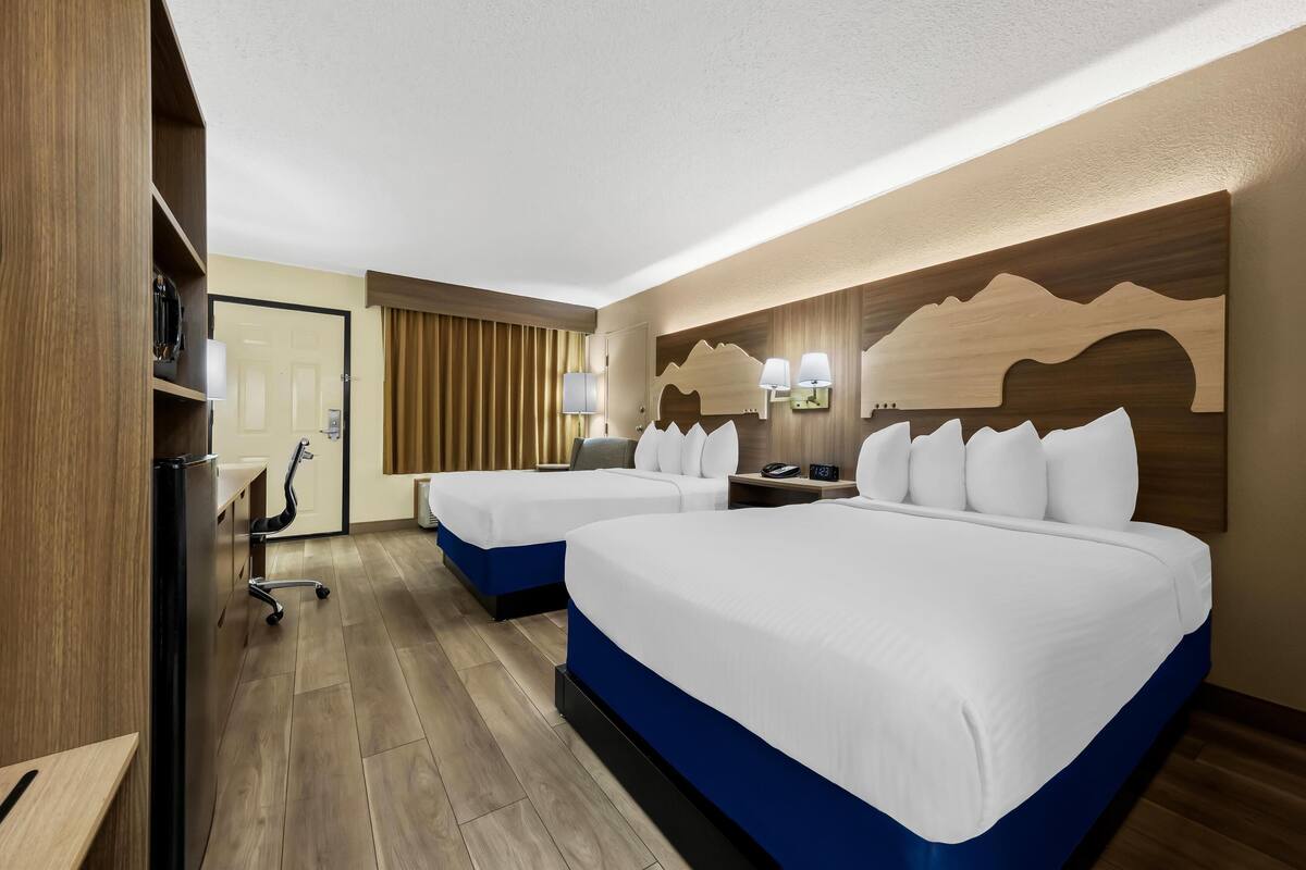 Quarto de hotel com duas camas, uma escrivaninha, uma cadeira e um guarda-roupa.