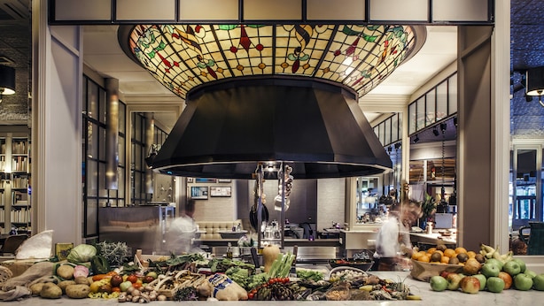 Uma cozinha com um teto de vitrais grande e colorido, bancada de mármore com produtos frescos e um exaustor moderno de aço inoxidável.