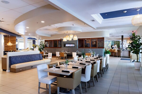 Um restaurante moderno com um balcão comprido, várias mesas e uma área de estar com sofás.