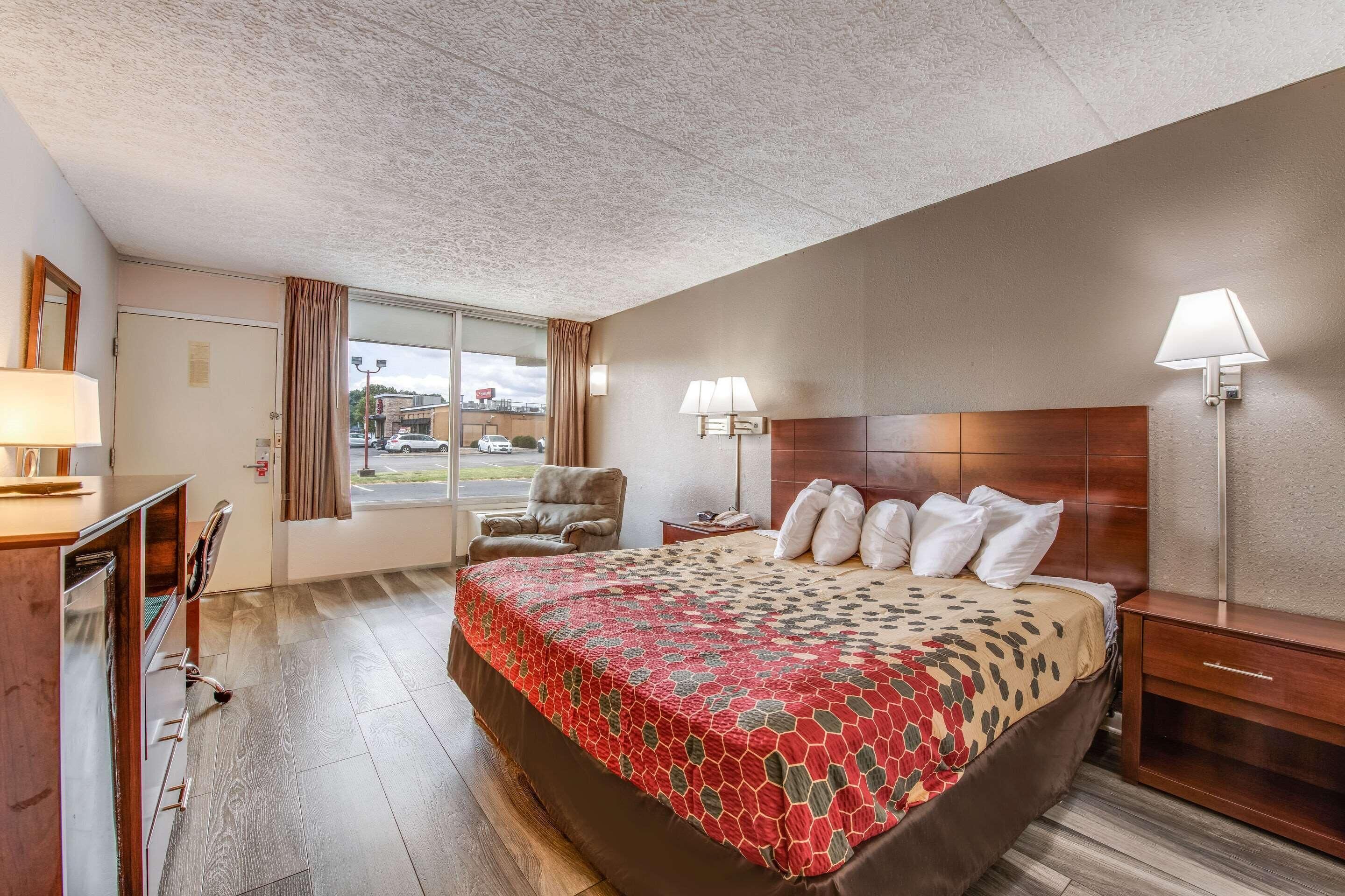 Quarto de hotel com uma cama, duas luminárias laterais, uma escrivaninha com luminária, uma cadeira e vista para o exterior.