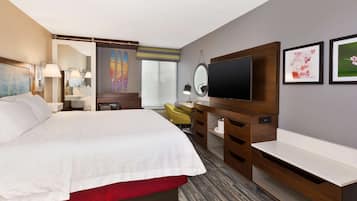 Quarto de hotel com uma cama grande, uma escrivaninha, televisão e obras de arte nas paredes.