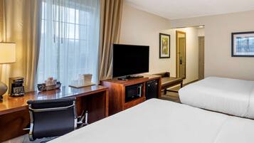 Quarto de hotel com uma cama, uma escrivaninha com cadeira, televisão e minibar.