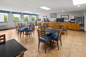 Uma sala de jantar com mesas e cadeiras, um espaço de cozinha com eletrodomésticos e janelas amplas com vista para o verde.
