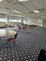 Uma sala de conferências com carpete estampado, mesas, cadeiras e um quadro branco.