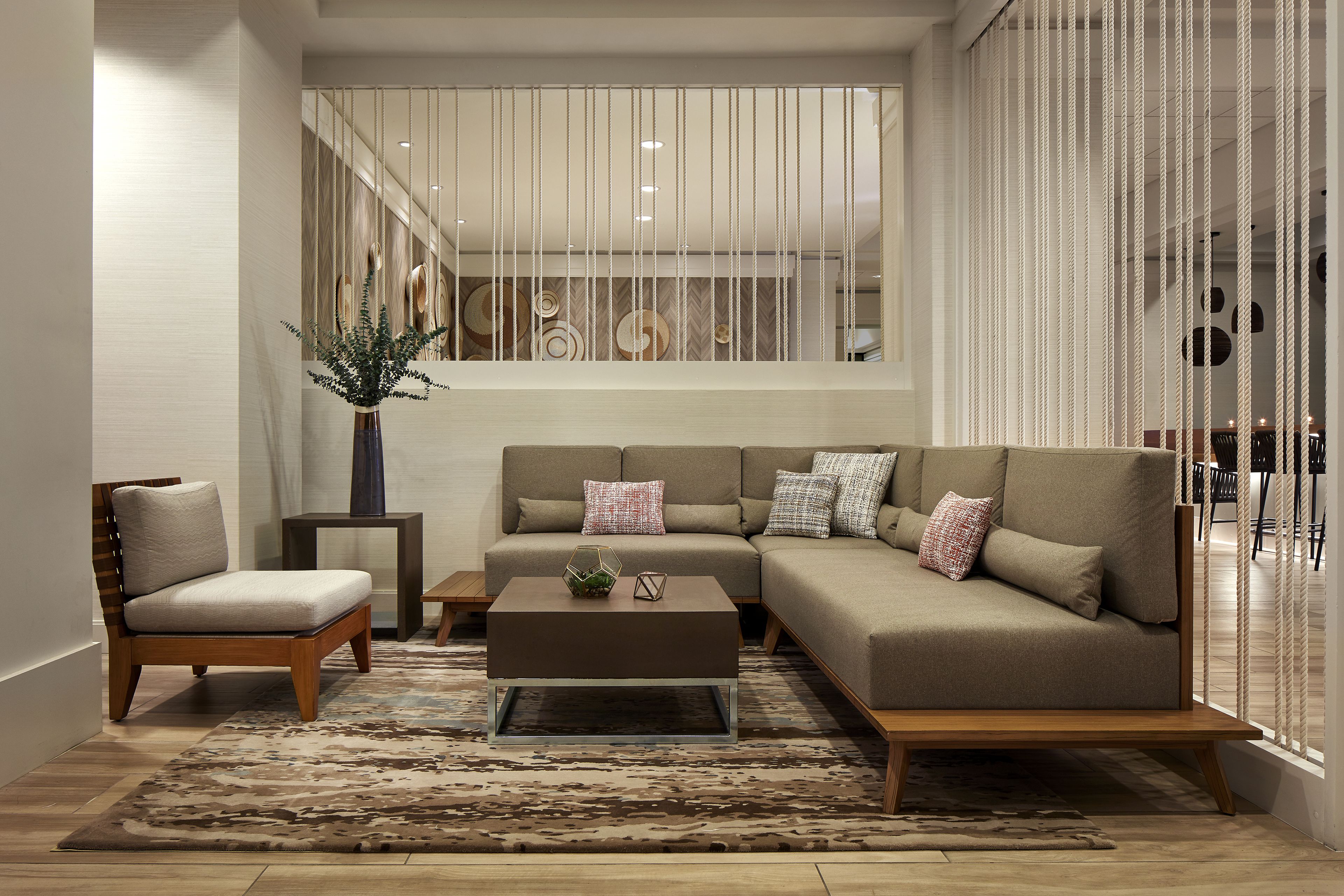 Uma sala de estar moderna com um sofá, uma mesa de centro e uma poltrona. Há uma planta decorativa e um tapete no chão.