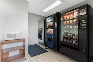 Espaço com máquinas automáticas de venda, incluindo um micro-ondas numa prateleira, máquina de bebidas geladas e máquina de snacks.