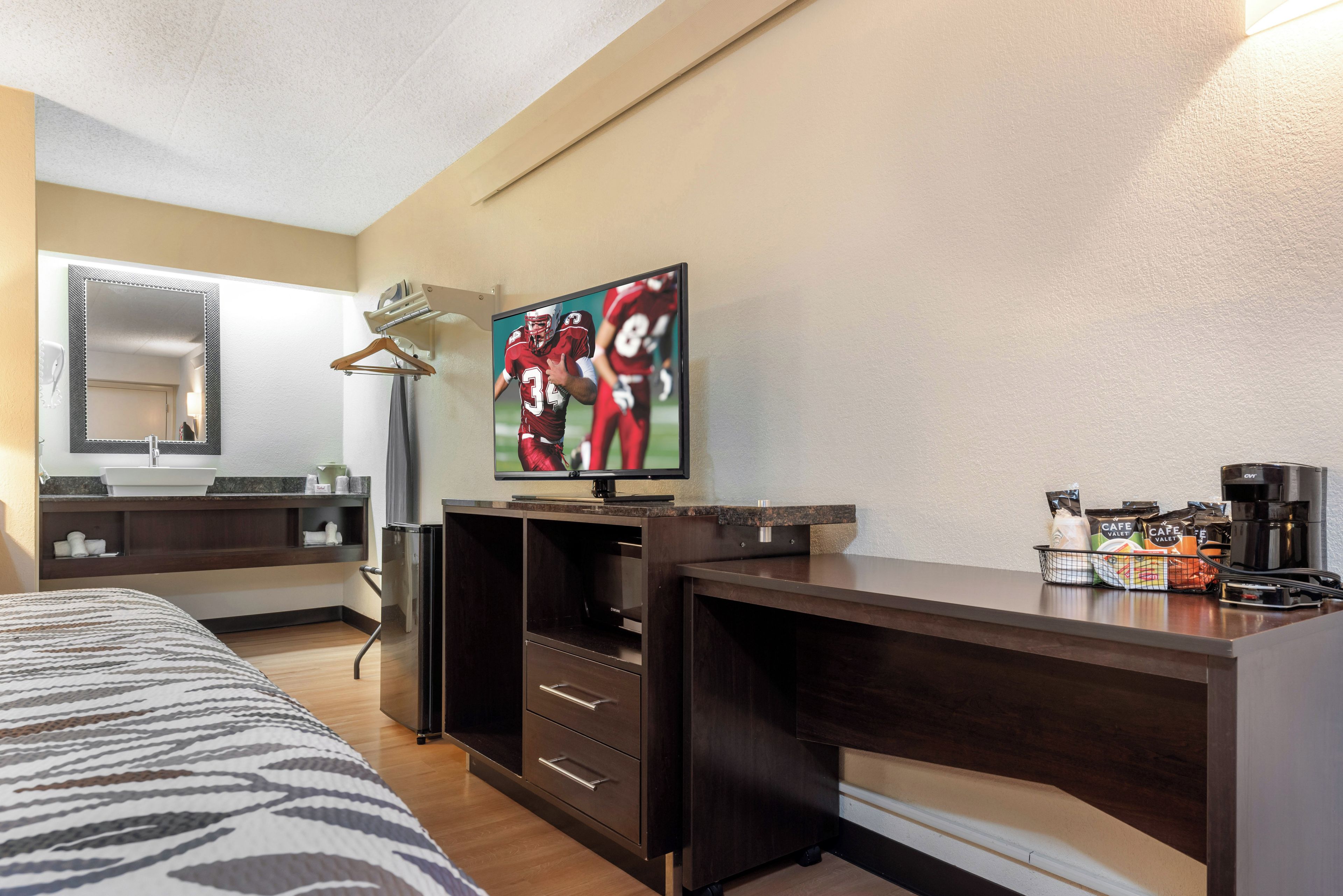 Quarto de hotel com cama, escrivaninha, televisão de tela plana, espelho, minibar e máquina de café.