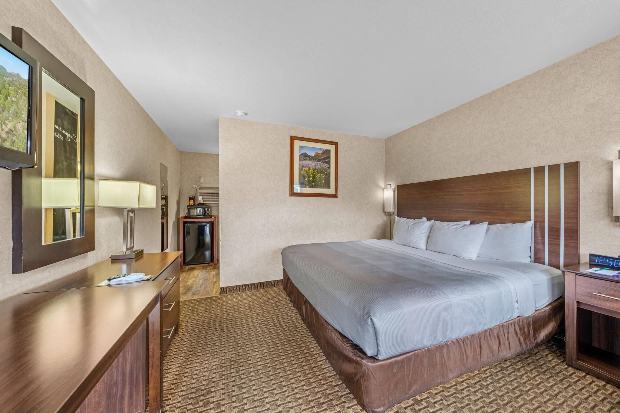 Quarto de hotel com uma cama grande, uma escrivaninha com luminária, uma mesinha pequena e um quadro na parede.