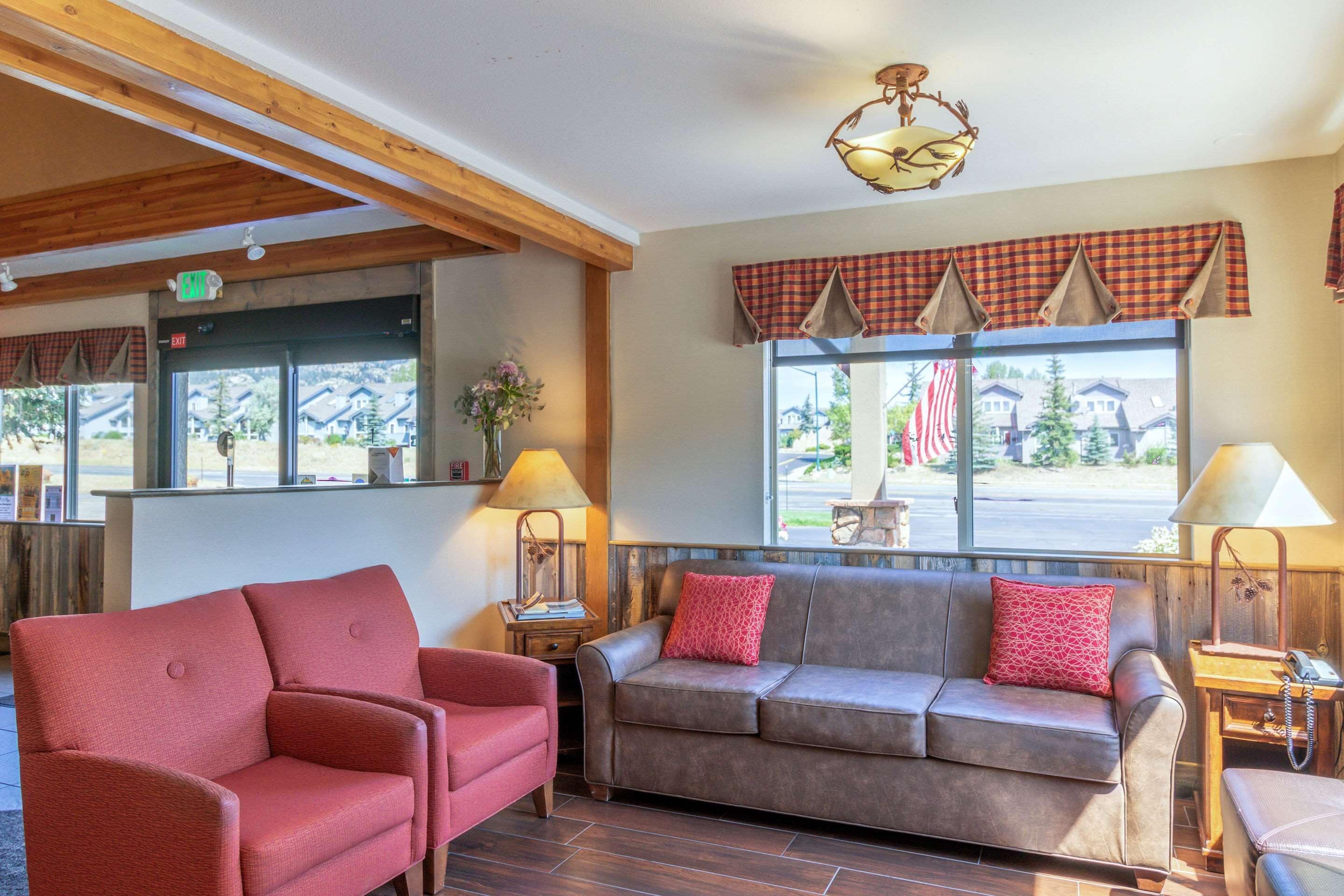 Um lobby acolhedor com um sofá vermelho e cinzento, uma poltrona vermelha e uma receção em madeira.