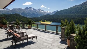 Um terraço com área de estar ao ar livre, vista para um lago e montanhas ao fundo.